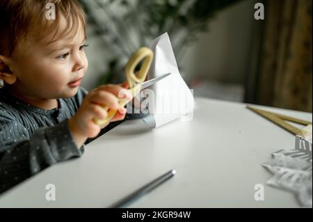 Baby boy with scissor cutting paper at table Stock Photo - Alamy