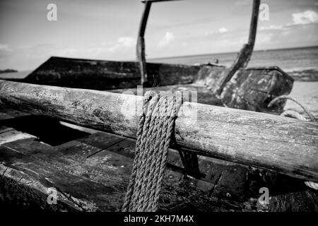 A grayscale shot of a wooden boat moored on the white beach in Zanzibar ...