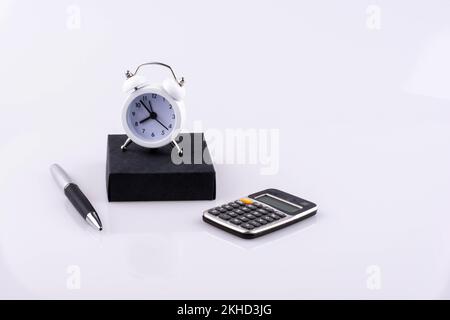 Alarm clock, calculator, pen and a notebook placed on a white ...