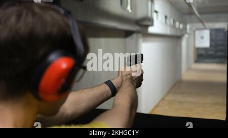 Guy in tactical headphones aiming pistol at target in shooting range ...