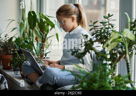 Schoolgirl in eyeglasses concentrating on her online work on laptop ...