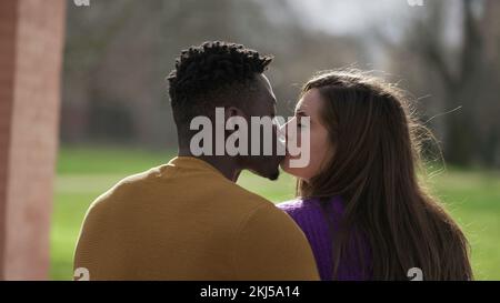 Back of interracial couple at park bench. Girlfriend kissing boyfriend ...