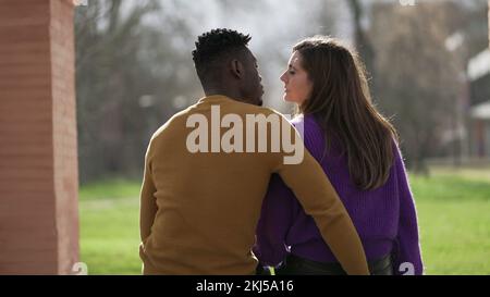 Back of interracial couple at park bench. Girlfriend kissing boyfriend ...