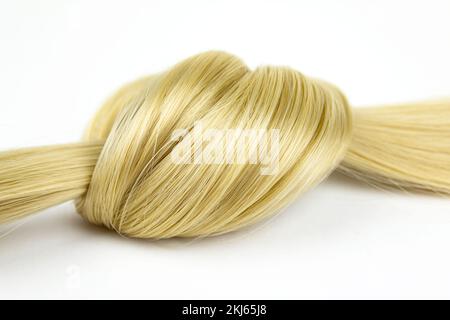 Strand of blond silky hair lock tied in knot on a white background ...