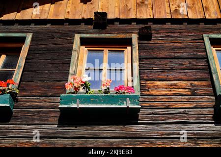 rustic alpine cabin or log cabin with geraniums on the window ledge in ...