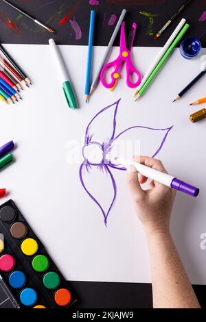 Vertical image of hand drawing purple flower on paper and art materials ...