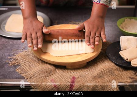 A closeup shot of a woman stretching a dough with a rolling pin on a ...