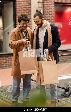 cheerful gay boyfriends in trendy clothes standing with shopping bags ...