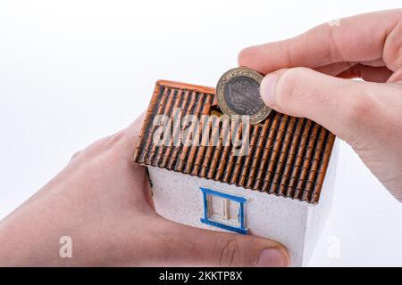 Hand dropping coin into the moneybox in the shape of a model house ...