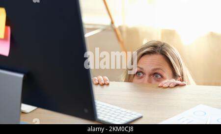 Surprised excited woman peeping out table and looking at pc screen ...