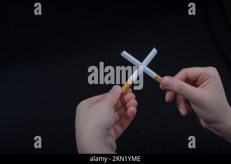 Hand is holding crossed cigarettes on black background Stock Photo - Alamy