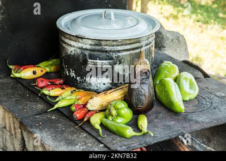 Roasting peppers and eggplant on iron plate on outdoor rustic hearth ...
