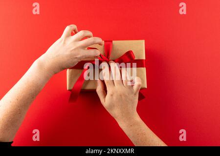 Overhead of hands tying gift in brown paper with red ribbon, on red ...