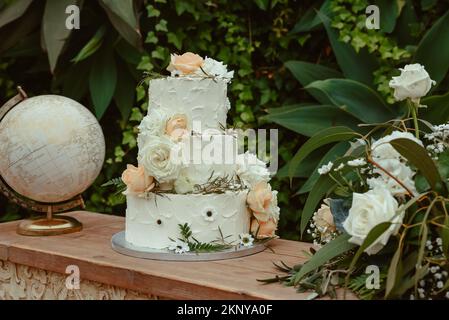 A flower bouquet, three tire cake and globe on wooden table with green ...