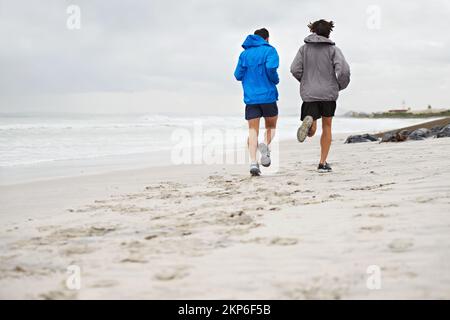 Getting fit with a friend. Rearview shot of two men jogging together ...