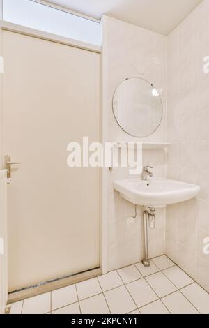 Cupboard with sink and mirror attached to tiled wall near door and ...
