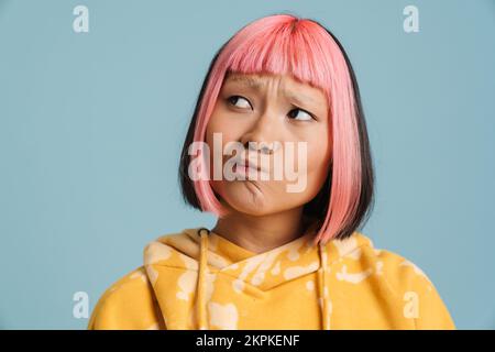 Asian girl with pink hair frowning and plugging her ears isolated over ...