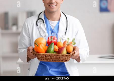 Male doctor holding basket with vegetables and vitamins on white ...