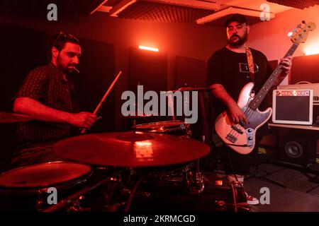 Male professionals playing bass guitar and drums in garage with neon ...