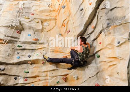 Man climbing on man-made cliff in the sport centre Stock Photo - Alamy