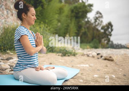 Concentrated woman sitting in lotus position yoga at summer garden park ...