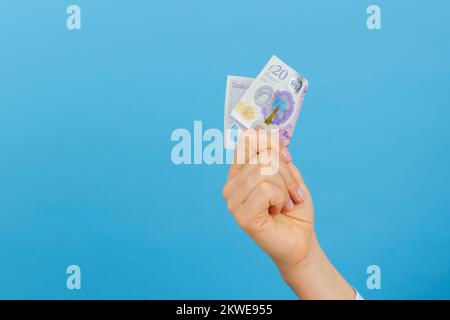 Woman's hand holding twenty british pounds banknote isolated on blue ...
