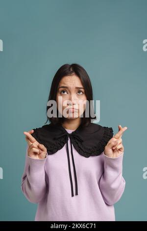Young asian woman frowning while fingers crossed for good luck isolated ...