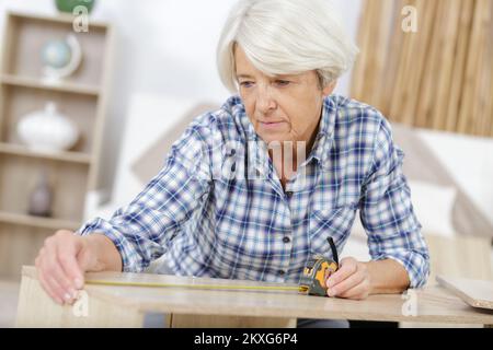 Mature woman measuring wooden furniture with tape in a well-organized ...