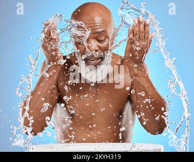 Water splash, skincare and face of senior black man in studio isolated on a blue background ...