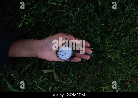 Womans hand laying on the grass holding a silver victorian pocket watch ...