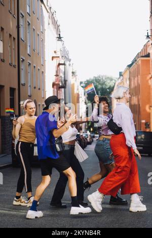 Young LGBTQIA friends walking on footpath during gay pride parade Stock ...