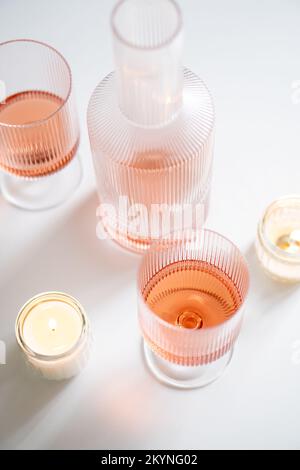 Rose wine in trendy ribbed wineglasses and decanter on white table ...