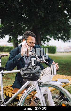 smiling businessman sitting on bicycle in office and looking at camera ...