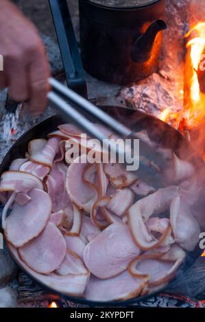 Australian style bacon being cooked over a camfire with silver tongs ...