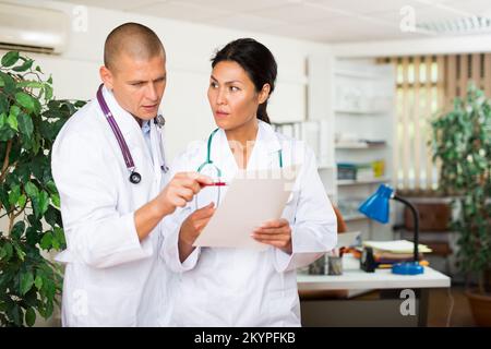 Two doctors discussing medical card of patient in office Stock Photo ...