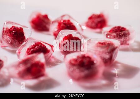 some frozen red raspberries inside ice cubes against white marble ...