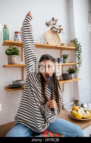 Funny beautiful woman singing into spatula, holding spatula as ...