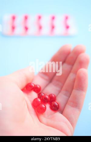 Round red vitamins in human fingers on pale blue background Stock Photo ...