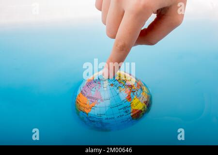 Little globe with finger on top floating in blue water Stock Photo - Alamy