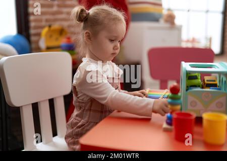 Adorable caucasian girl playing with truck toy sitting on table at ...