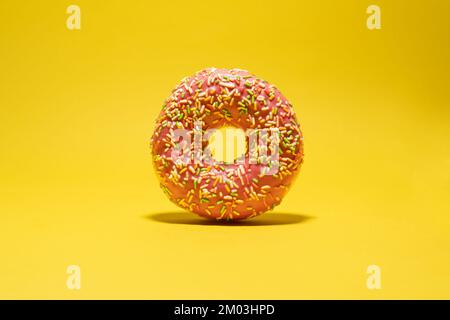 Pink donut with multicolored sprinkles on yellow background. Creative ...