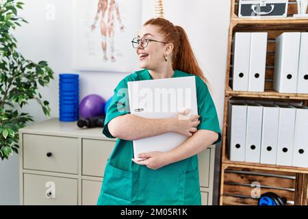 Young redhead woman wearing phsiologist uniform holding binder at ...