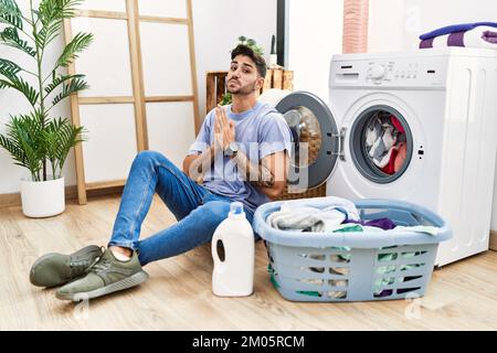 Young hispanic man putting dirty laundry into washing machine smiling ...