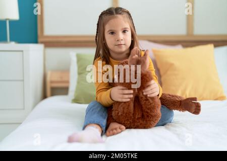Adorable hispanic girl hugging monkey doll lying on bed at bedroom ...