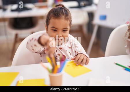 Adorable hispanic girl student sitting on table drawing on paper at ...
