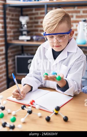 Adorable toddler student writing on notebook with doubt expression at ...
