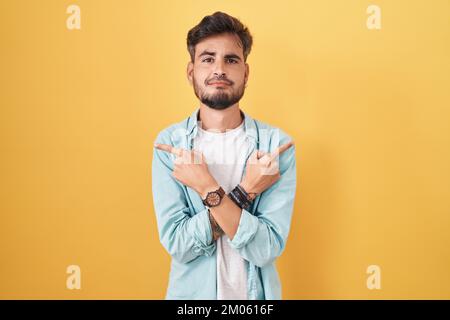 Hispanic man with tattoos standing over blue background pointing aside ...