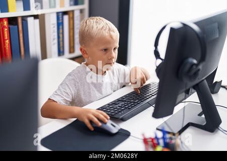 Adorable toddler student using computer sitting on table at classroom ...