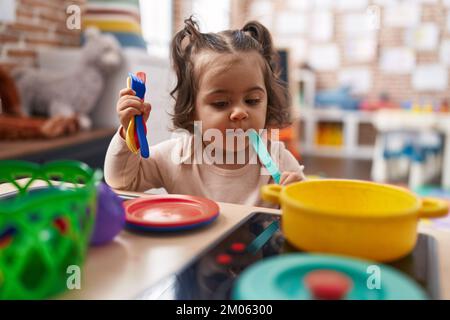 Adorable hispanic girl playing with play kitchen standing at ...