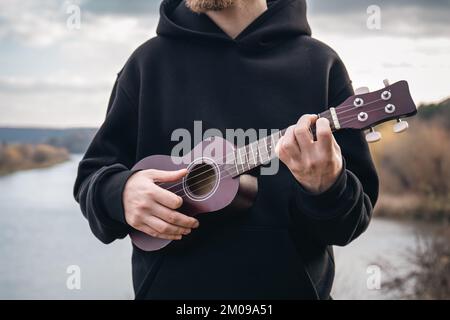 A man plays the ukulele guitar in nature, blurred background Stock ...